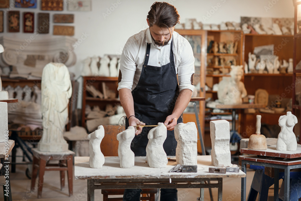 Male craftsman in working uniform makes a limestone copy of woman torso ...