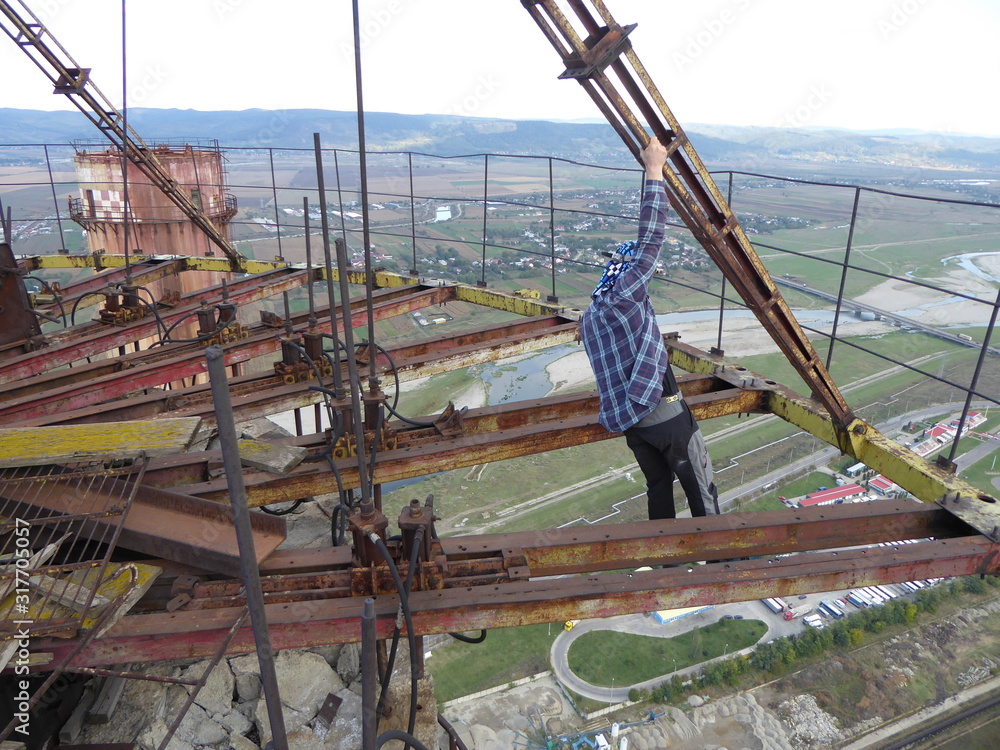 Athlete man hanging an iron rail on top of a tall industrial chimney ...