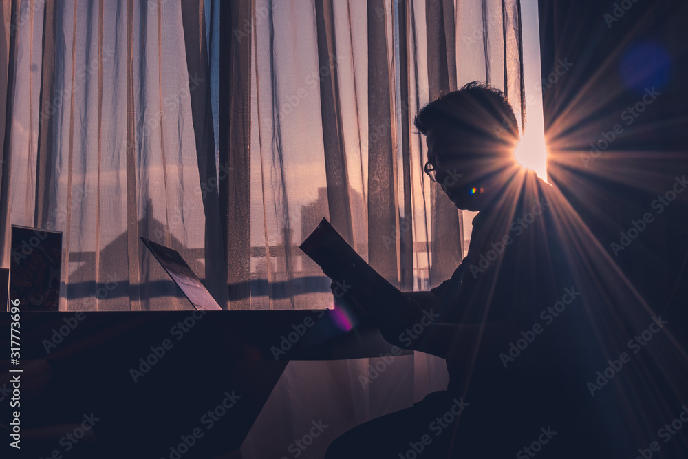 The silhouette of a man reading in a modern room against a window lit ...