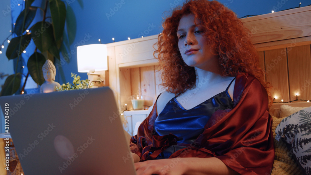 Portrait attractive curly pretty woman use laptop on the bed at night ...