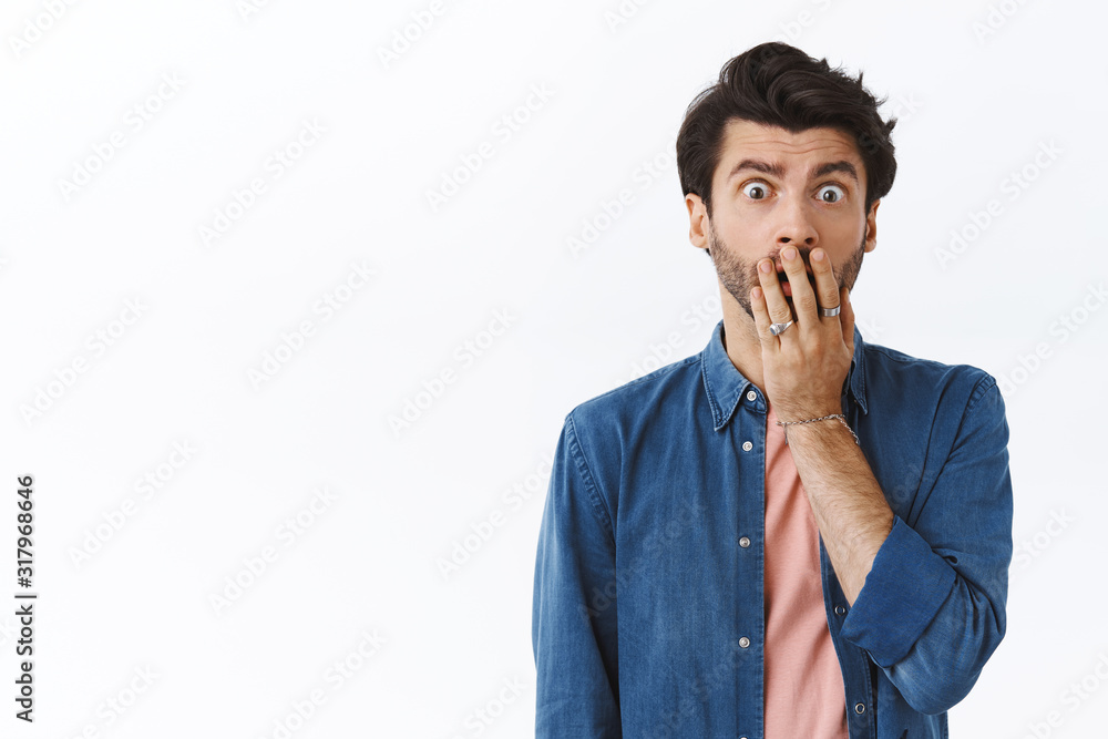 Troubled young bearded man, gasping cover opened mouth, stare worried ...