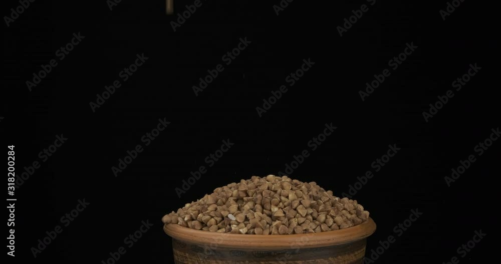 Whole grains of buckwheat fall on a bunch of grains lying in a clay pot ...