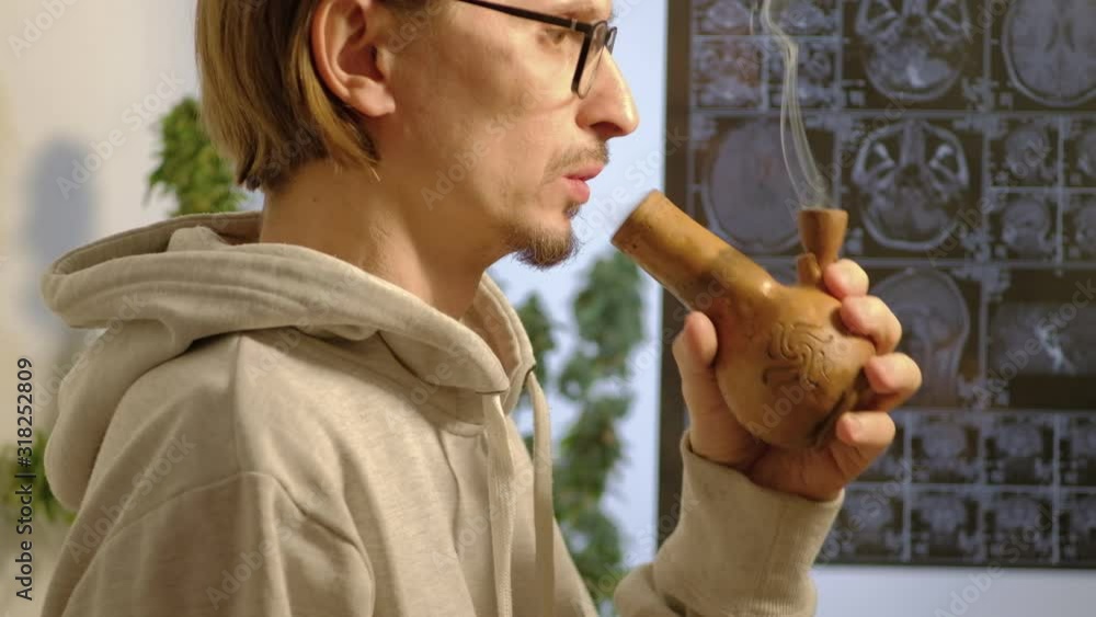 Vidéo Stock a sick European man in glasses smokes cannabis using bong ...