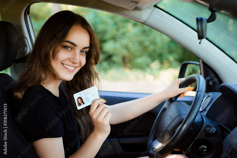 Smiling young female with pleasant appearance shows proudly her drivers ...