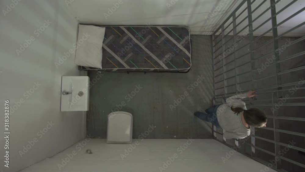 Female Prisoner in Prison Cell. The woman walks shakes the Jail door in ...