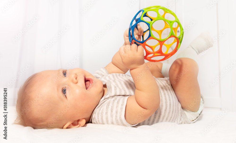 Little cute baby boy toddler play and hold toy ball laying on the back ...