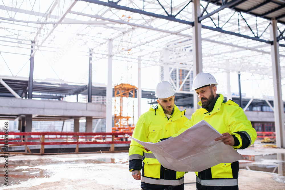 Men engineers standing outdoors on construction site, holding ...