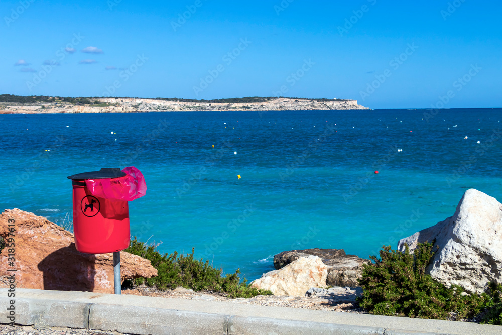 Red plastic waste bin for dog poop next to the public beach. Concept of ...