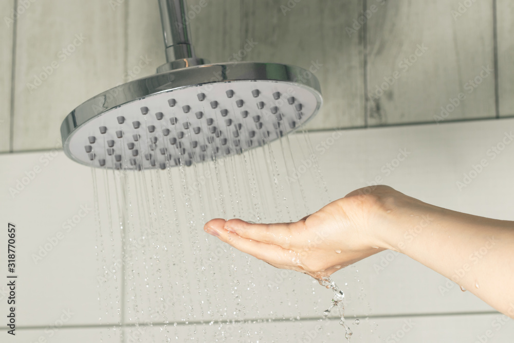 Female hand touching water pouring from a rain shower head, checking ...