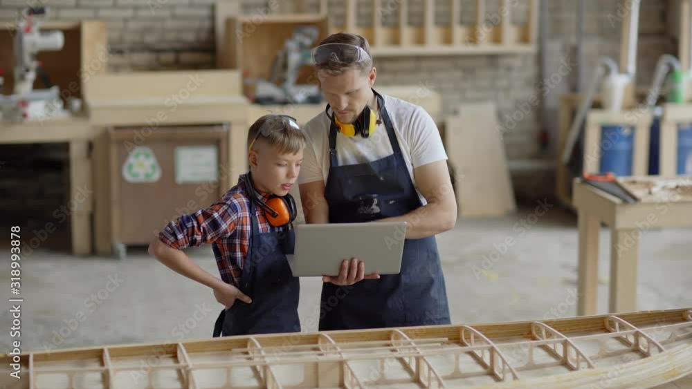 Vidéo Stock Middle aged carpenter and his son building wooden boat ...