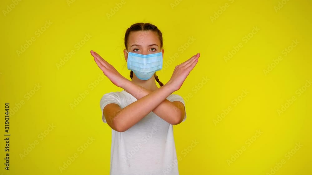 Teen girl in medical mask looks at camera and keeps her arms crossed ...