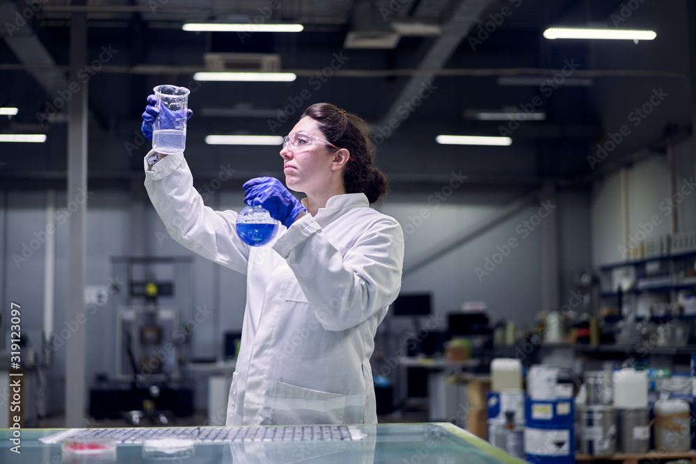 Lab girl in glasses and white coat with flask with blue liquid in her ...