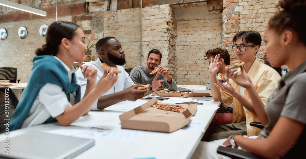 Happy team relaxing at work. Positive multicultural team eating pizza ...
