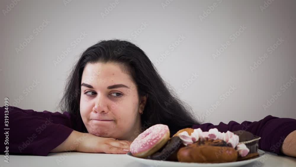 Portrait of obese Caucasian brunette girl taking dessert from plate and ...