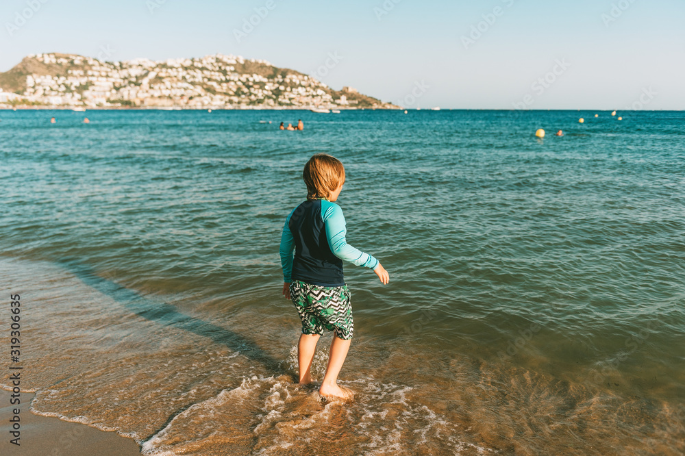 Funny little boy playing by the sea, wearing sun safe rash vest, family ...