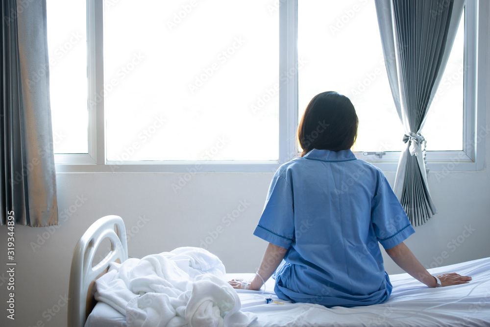 Back view of patient woman sitting on bed in hospital ward, looking ...
