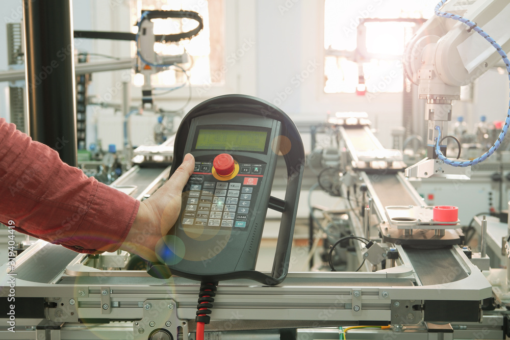 Close up of man's hand holding teach panel to control robot arm which ...