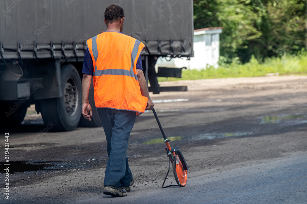 Road worker measuring a road section for asphalting with a surveyor's ...
