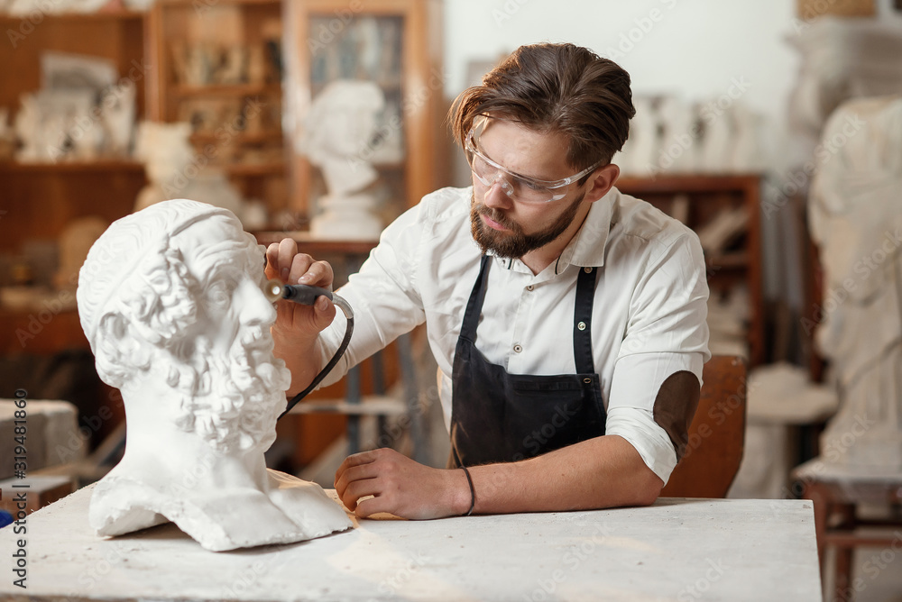 Male sculptor repairing gypsum sculpture of woman's head at the working ...