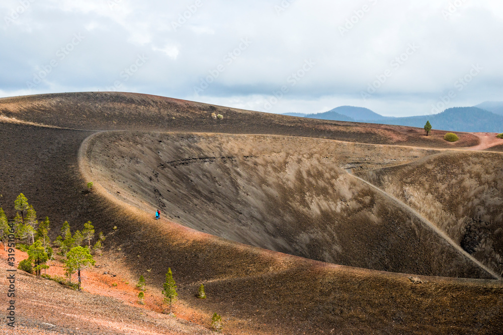 Two people hike along the crater rim of Cinder Cone volcano on a ...