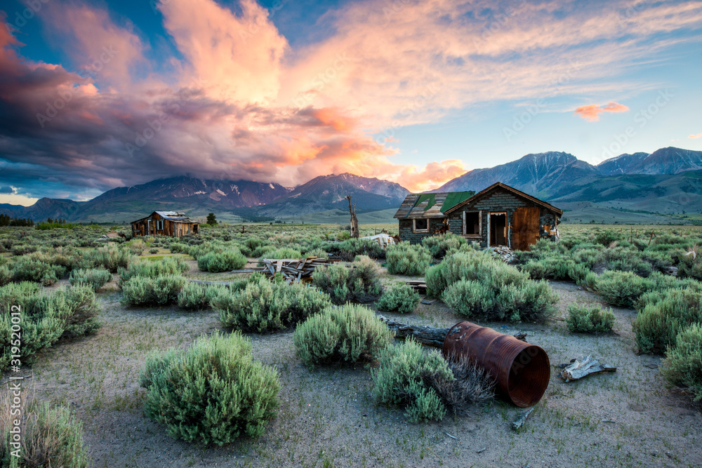 A magnificent sunset explodes over old abandoned cabins in the desert with the Sierra Nevada ...
