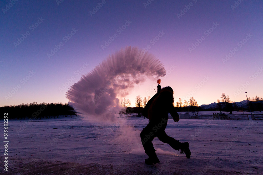 A silhouette man throws boiling water in the air. Rapid freezing ...