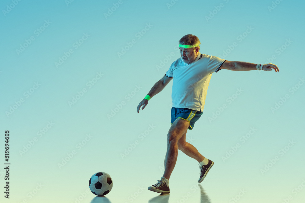 Senior man playing soccer, football on gradient background in neon ...