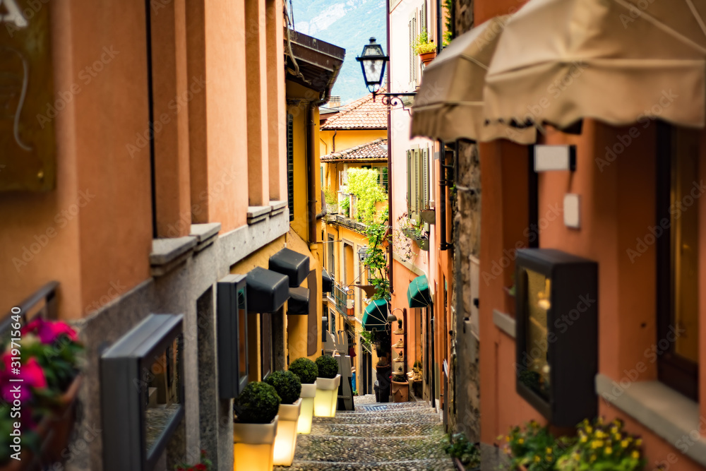 Narrow street with orange buildings and lanterns in Bellagio town at ...