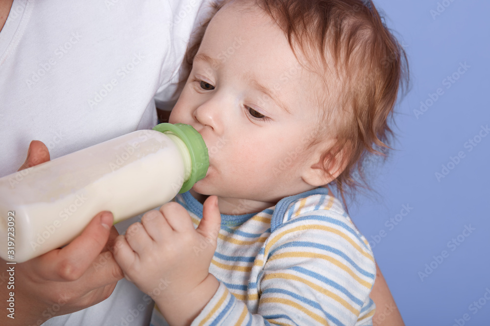 Image of baby drinking milk and looking at his bottle, isolated over ...