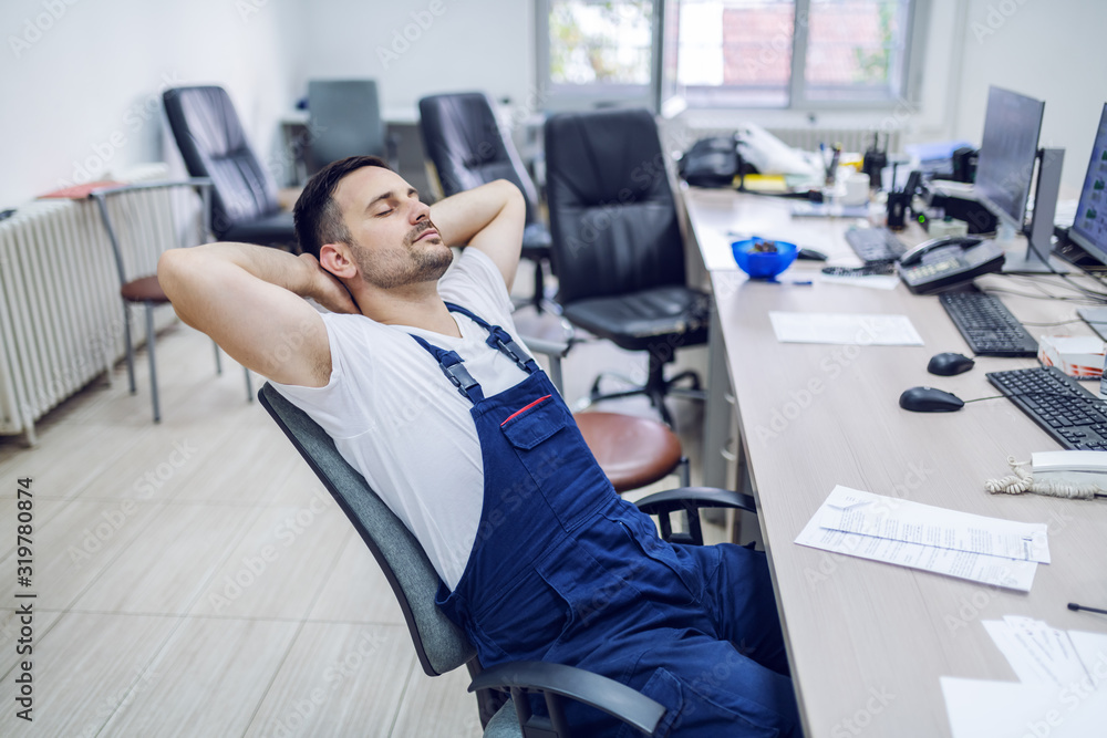 Lazy factory worker sitting on chair with hands behind head and ...
