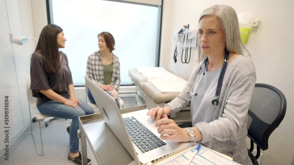 Female doctor working at laptop with mother and daughter patient ...
