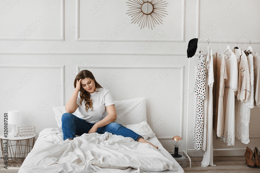 Plus-size model girl in jeans and white t-shirt sitting on bed near ...