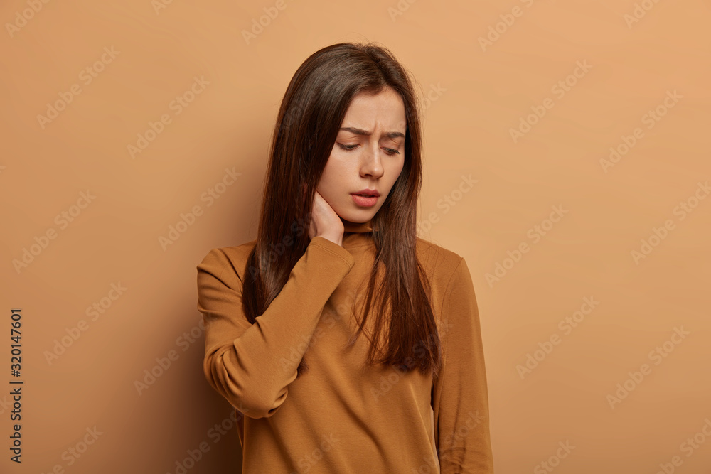 Displeased sad woman touches neck, looks down with unhappy expression ...
