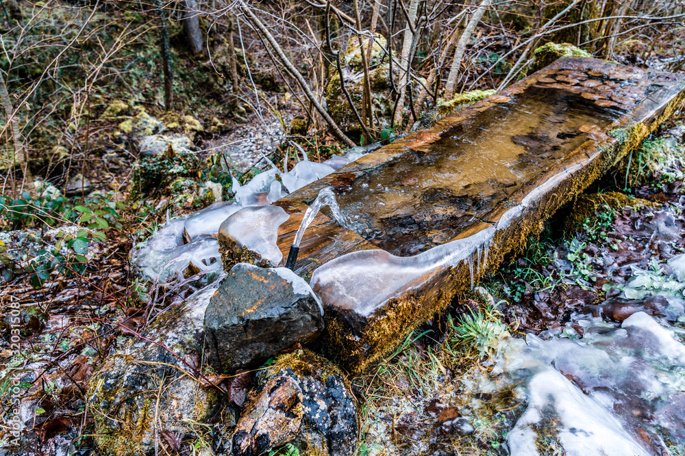 Brunnen im Winter mitten in Gebirgsschlucht, Holztrog der eine Quelle ...
