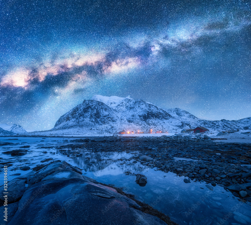Milky Way over snow covered mountains and rocky beach in winter at ...