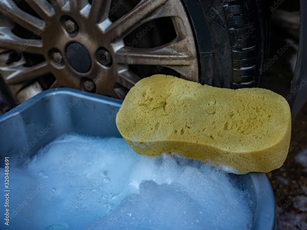 Yellow sponge on a bucket of soapy water in front of a dirty rear alloy ...