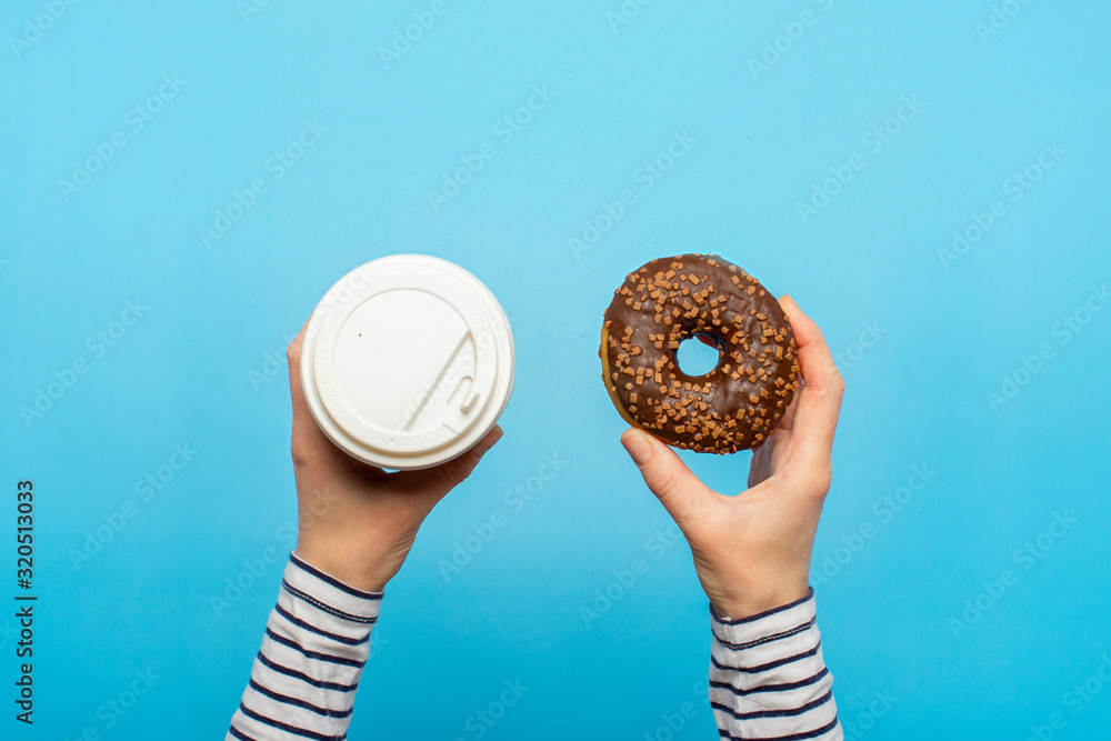 Female hands hold a donut and a paper cup with coffee on a blue ...
