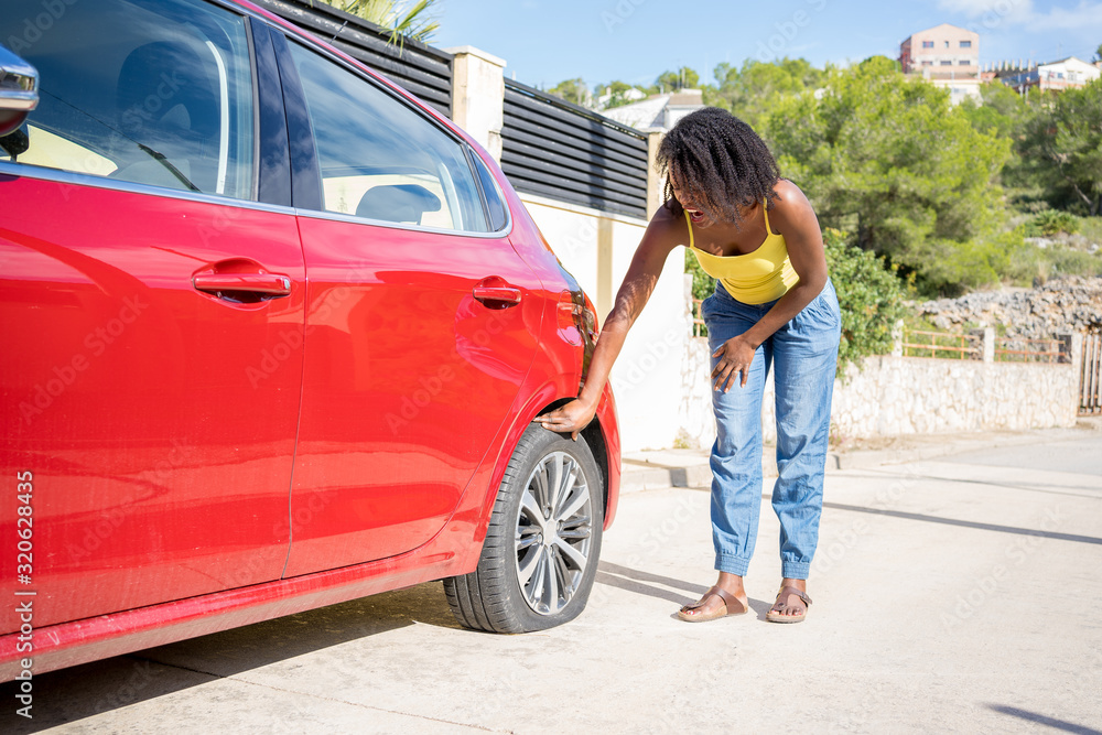 Afro woman very concerned to find out she has a flat tire on her red ...
