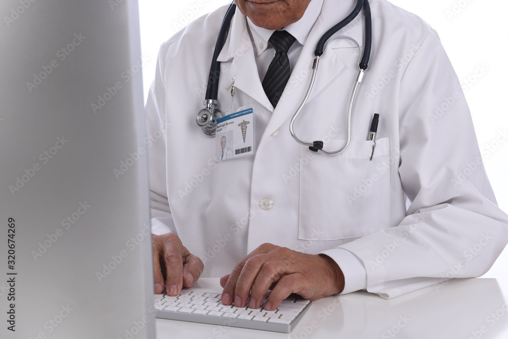 Closeup of a docor partially behind his computer screen as he types on ...