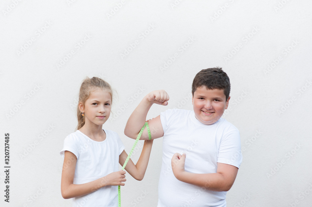 thin little girl in white jersey measuring fat thick smiling boy muscle ...
