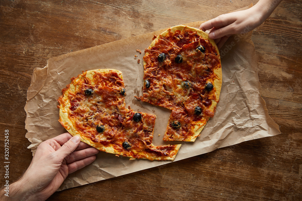 Cropped view of couple holding delicious Italian pizza in broken heart ...