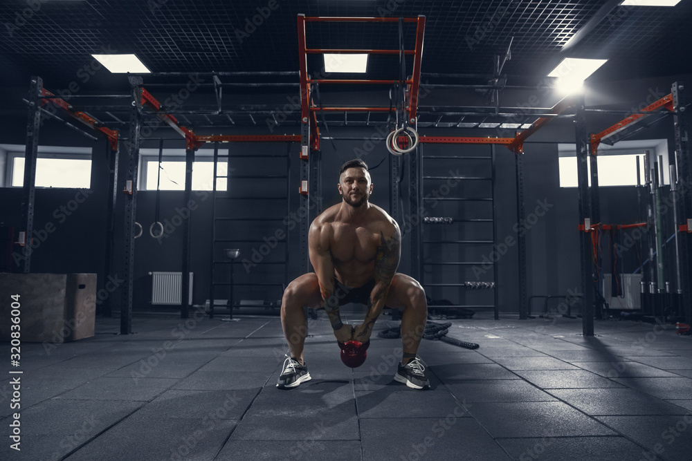 Unstoppable. Young muscular caucasian athlete practicing squats in gym ...