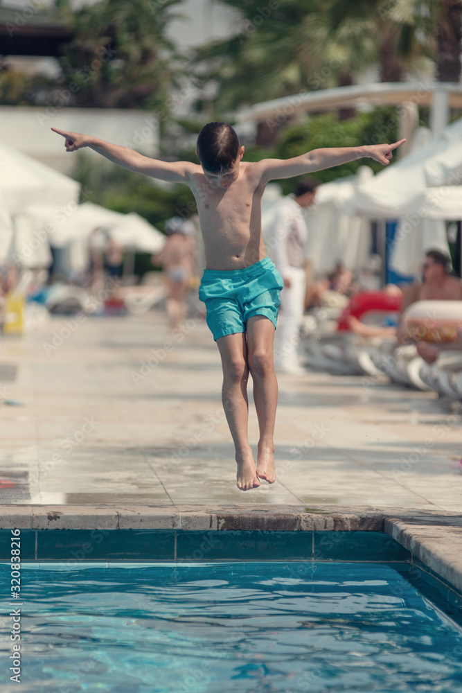 Caucasian boy having fun making high jump to plunge into swimming pool ...