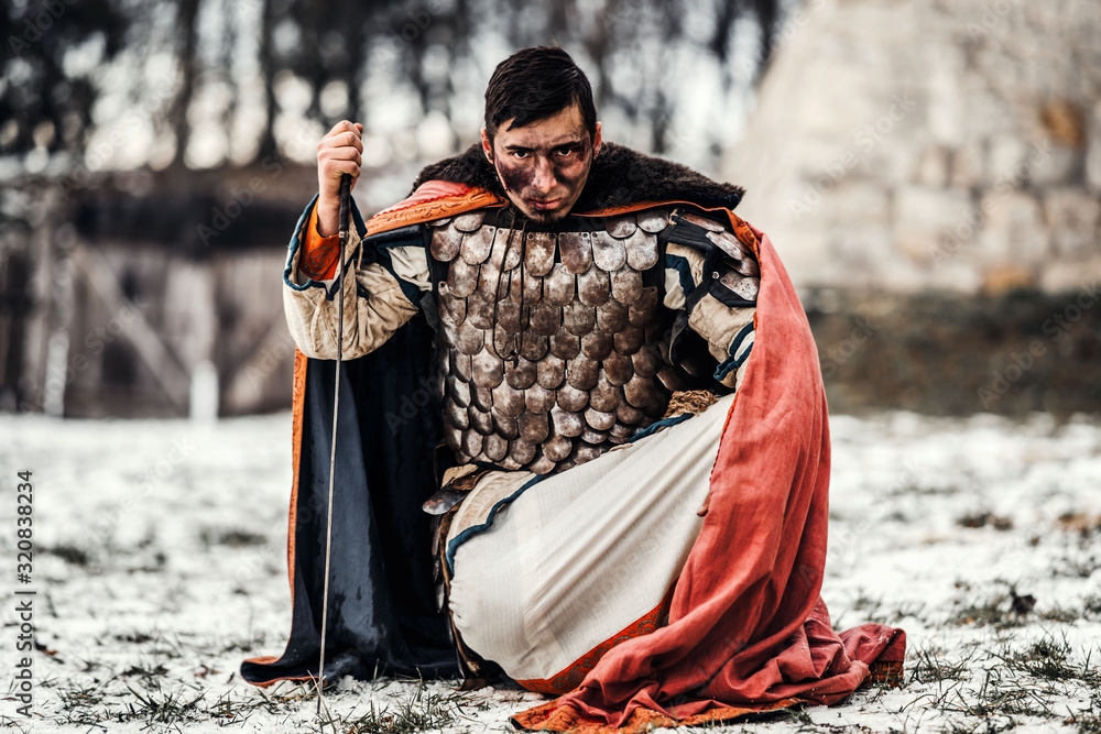A medieval warrior in chain mail armor and mantle kneeling and holds ...