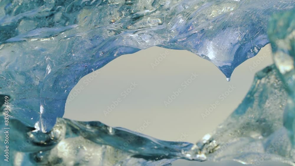 Zoom out from hole in transparent, shiny piece of ice melting. Concept ...