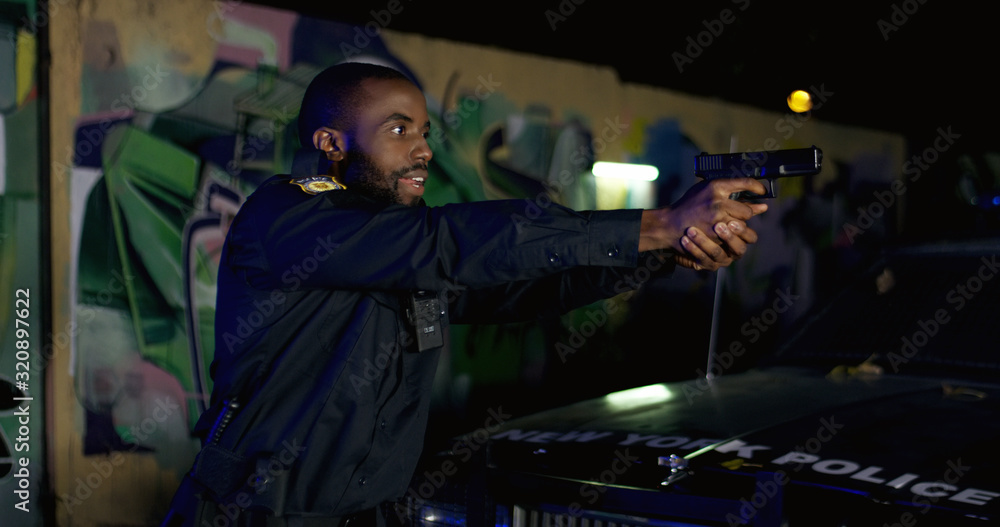 Side view on African American young cop pointing gun at somebody ...