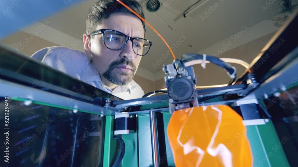 3D printer printing an object from plastic. Male engineer is looking ...