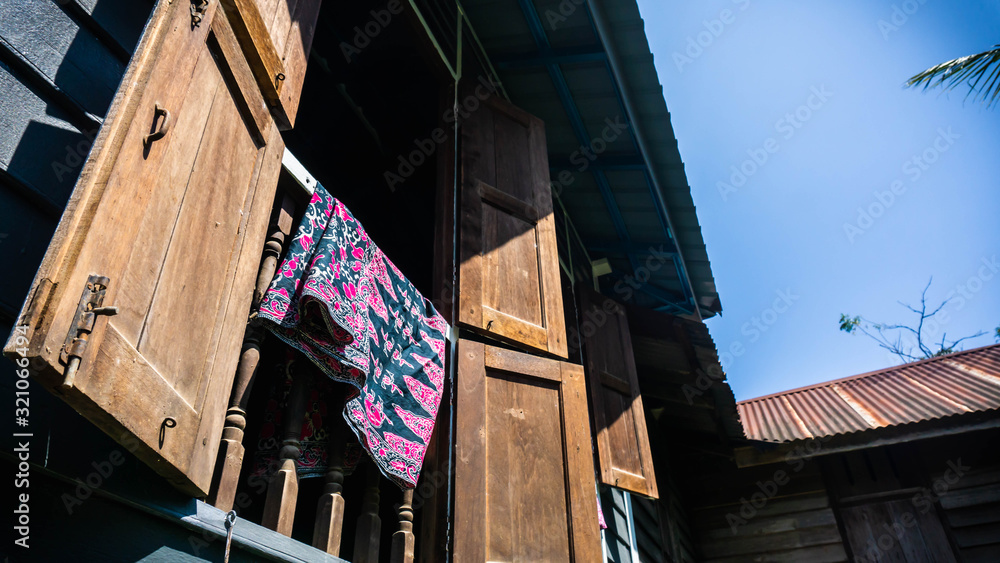 Batik fabric hanging on the window of Rumah Kampung under the bright ...