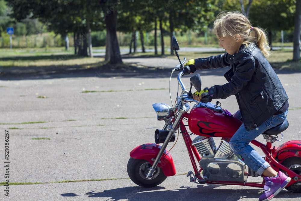 little girl biker child in a leather motorcycle jacket rides a children ...