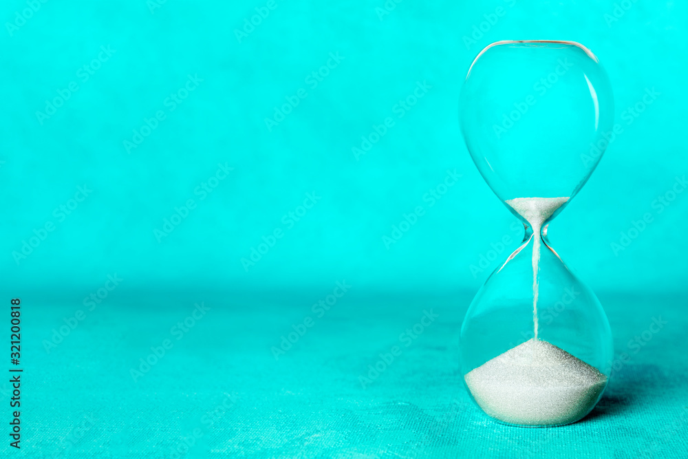 Hourglass with sand falling through, side view on a vibrant blue ...
